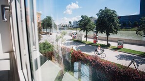 Vista da janela para uma rua da cidade, com rio, árvores e um ciclista.