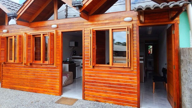 Uma cabana de madeira com telhado inclinado, janelas amplas e uma área de cozinha visível.
