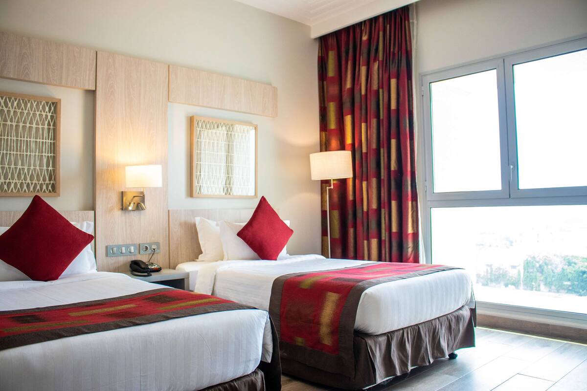 Quarto de hotel com duas camas, uma janela grande e vista para o exterior.