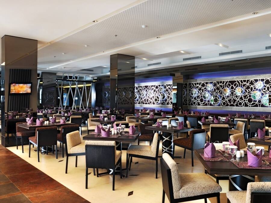 Um restaurante moderno com várias áreas de refeições, cada uma com mesas e cadeiras, e uma parede decorativa com padrão geométrico.