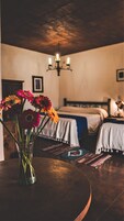 Quarto com duas camas, um candelabro e um vaso com flores sobre uma mesa.