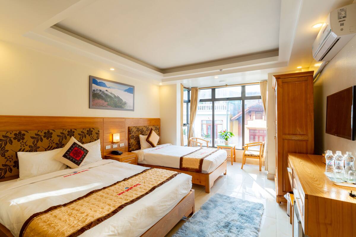 Quarto de hotel com duas camas, uma escrivaninha, uma cadeira e uma televisão.