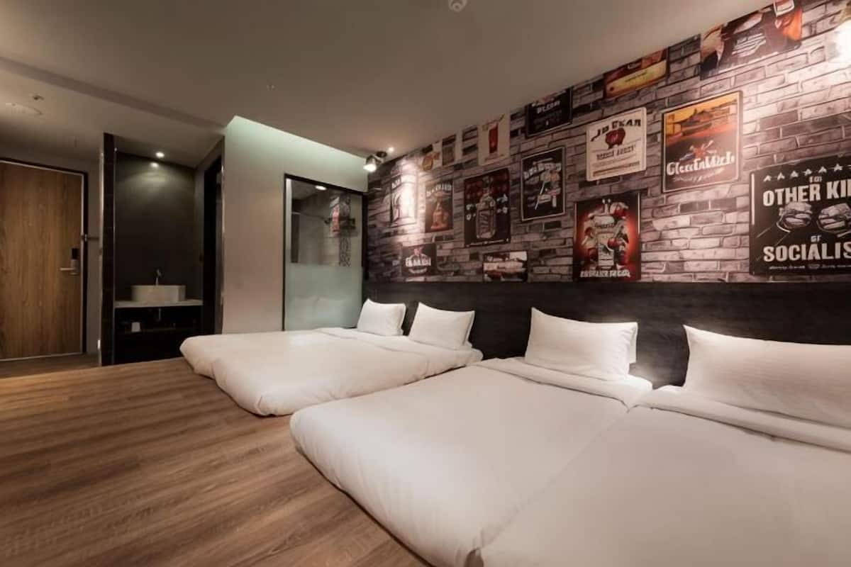 Quarto de hotel com duas camas, parede de tijolos, piso de madeira e banheiro pequeno.