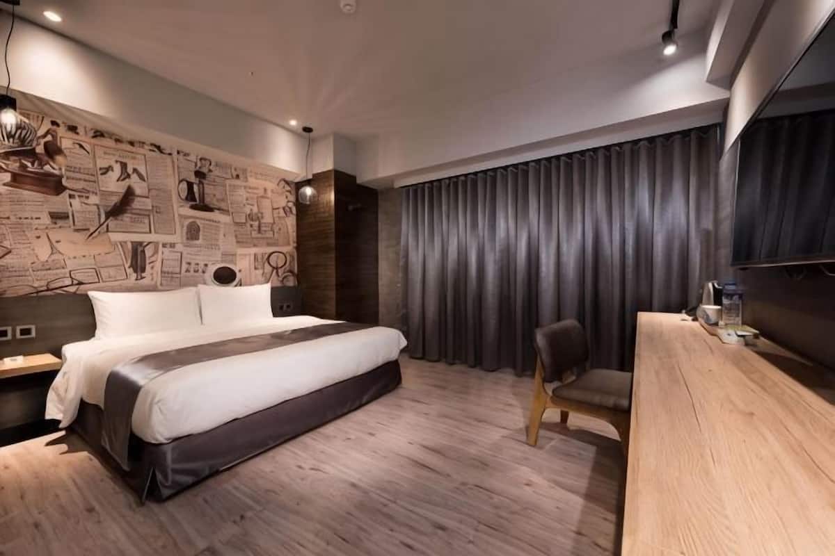 Quarto de hotel moderno com uma cama grande, uma escrivaninha, uma cadeira, uma cortina escura e um painel de parede com desenho.