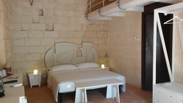Um quarto com parede de pedra, cama com cabeceira branca, mesas de cabeceira com abajures e um guarda-roupa.