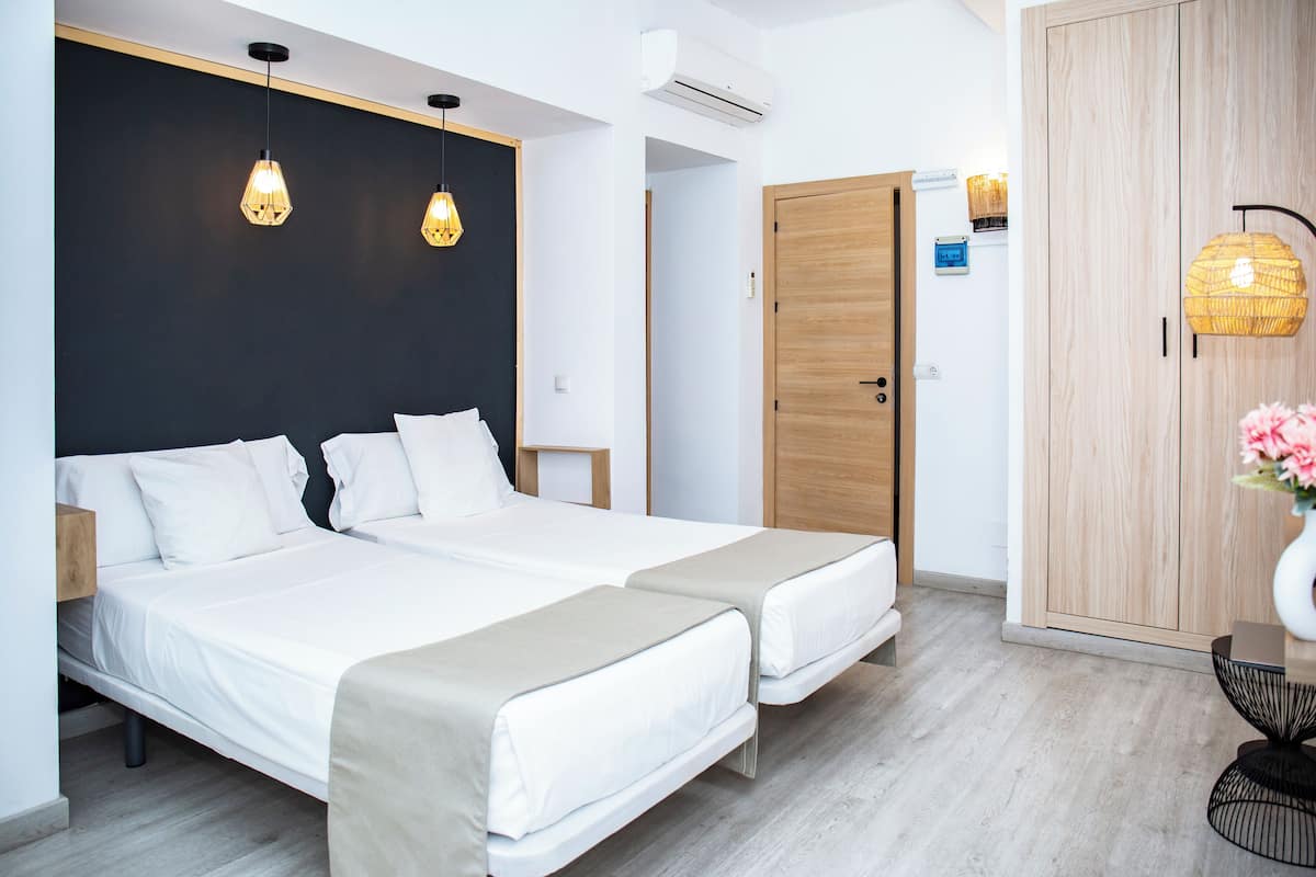 Quarto de hotel moderno com duas camas, um guarda-roupa de madeira e uma pequena mesa com um vaso.