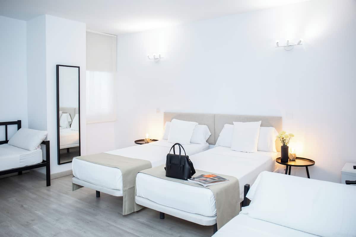 Quarto de hotel moderno com duas camas, um espaço de estar, um espelho grande e uma mesa de cabeceira com abajur.