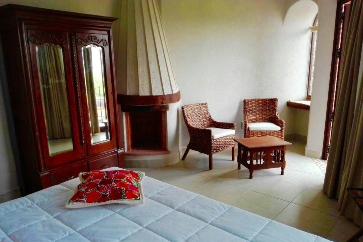 Quarto de hotel com uma cama, duas cadeiras de vime, um armário de madeira e uma mesinha.