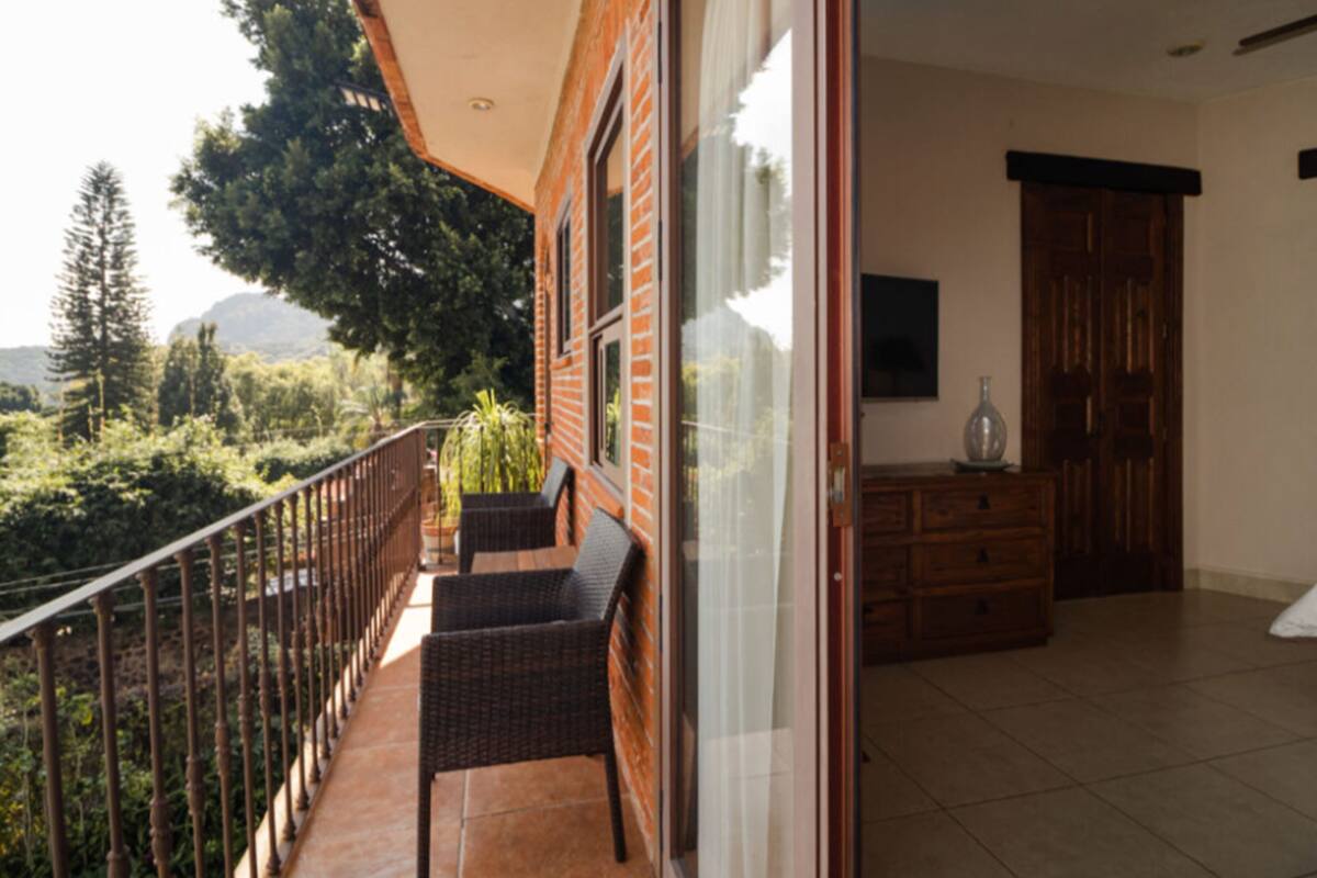 Uma varanda com mobiliário de vime, vista para o verde e um armário de madeira.