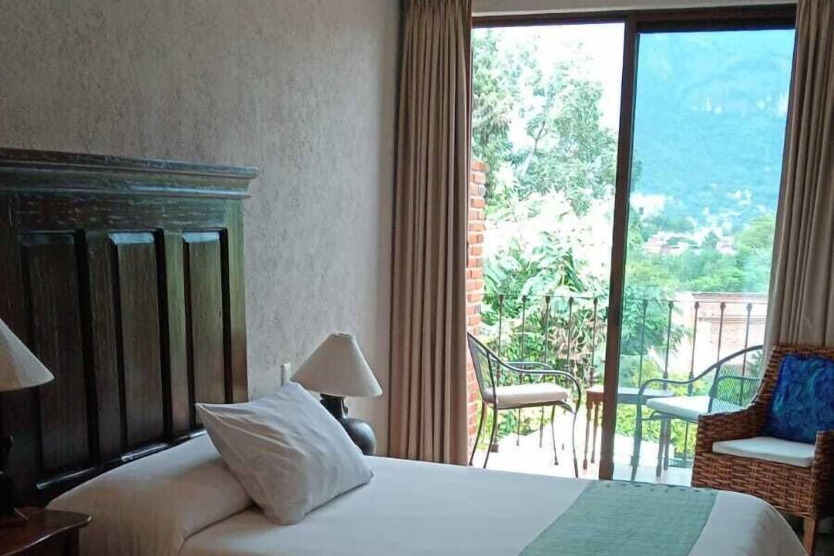 Quarto de hotel com uma cama grande, mesa de cabeceira, abajur, cadeira e vista para o exterior através de uma porta deslizante.