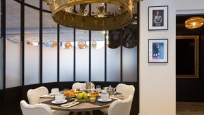 Uma área de refeições com uma mesa redonda posta para o café da manhã, com pratos, xícaras e diversos alimentos.