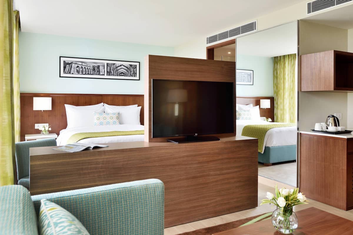 Quarto de hotel com cama, televisão, escrivaninha e área de estar.