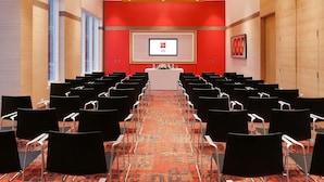 Uma sala de conferências com fileiras de cadeiras, um pódio e uma tela exibindo um logotipo.