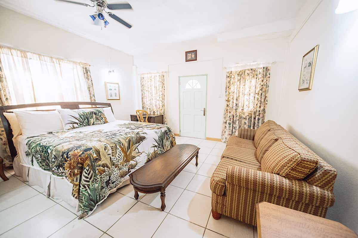 Um quarto com cama, um banco de madeira, um sofá e um ventilador de teto.