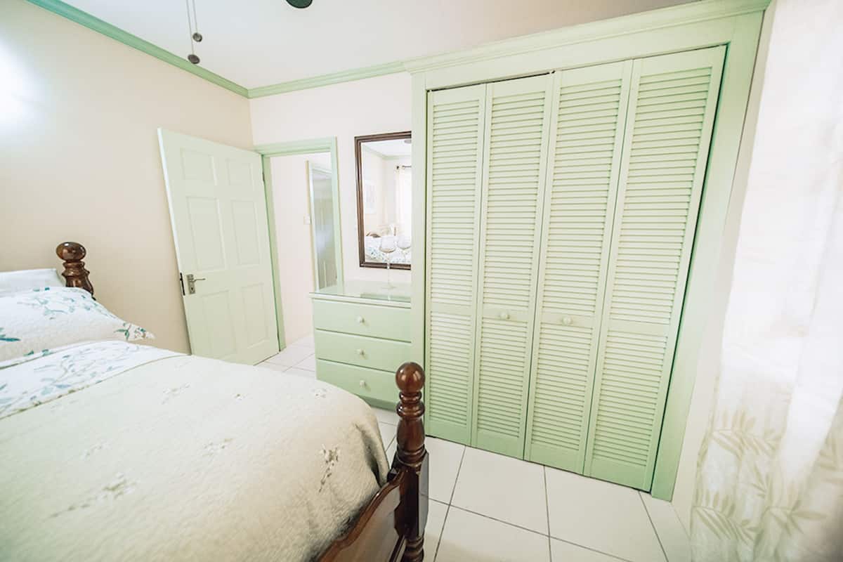 Quarto com cama, cômoda, espelho e armário verde.