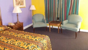Quarto de hotel com uma cama, duas poltronas, uma mesinha, um abajur e um edredom estampado.