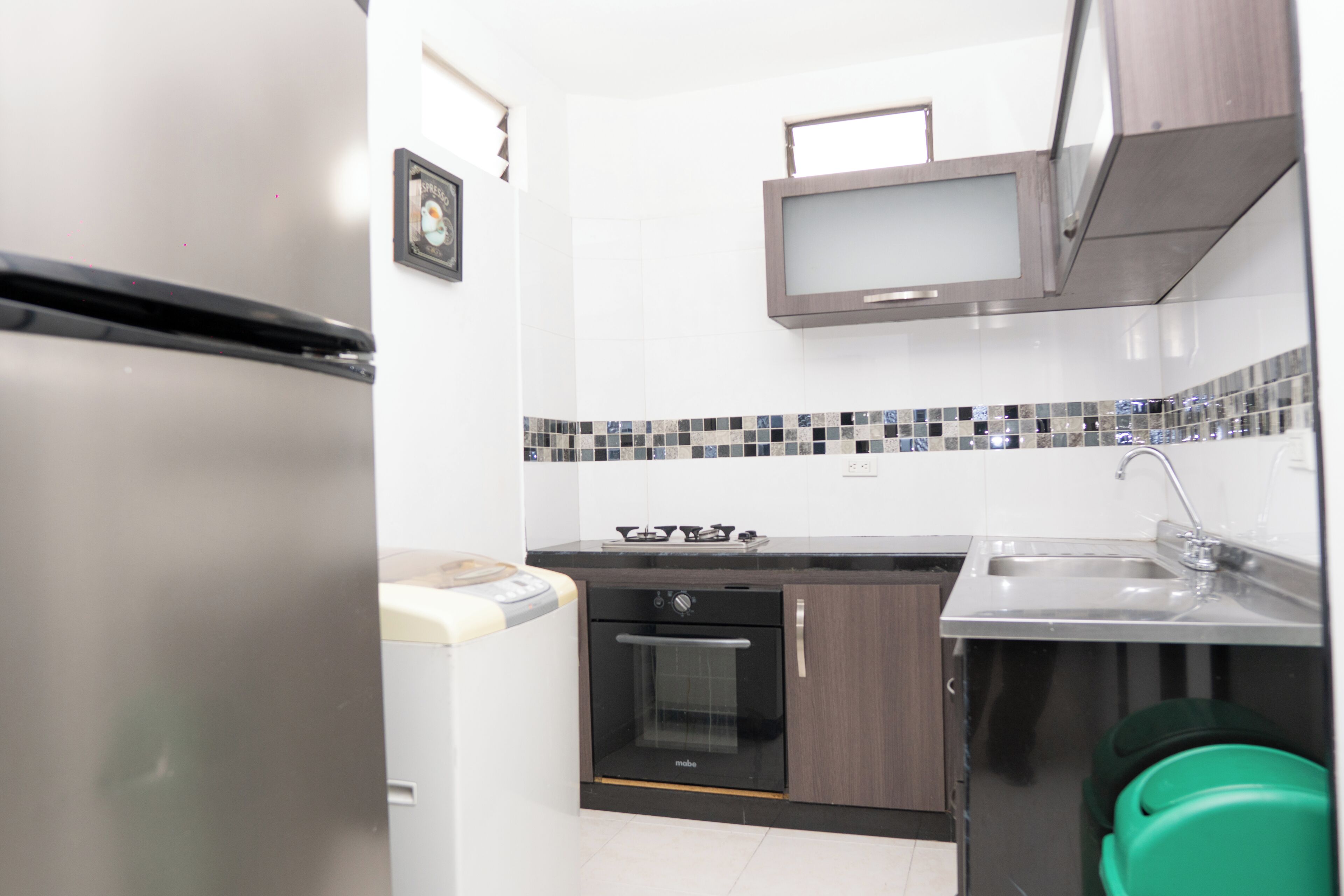 Cozinha compacta equipada com frigorífico, forno, micro-ondas e painel de azulejos.