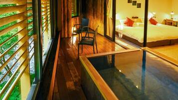 Quarto de hotel moderno com varanda envidraçada, piso de madeira e cama com roupa de cama branca e almofadas vermelhas.