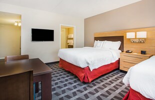 Quarto de hotel com uma cama grande, uma escrivaninha, uma televisão e um banheiro visível por uma porta aberta.