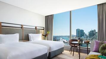 Quarto de hotel com uma cama grande, uma mesa pequena e vista para o horizonte da cidade.