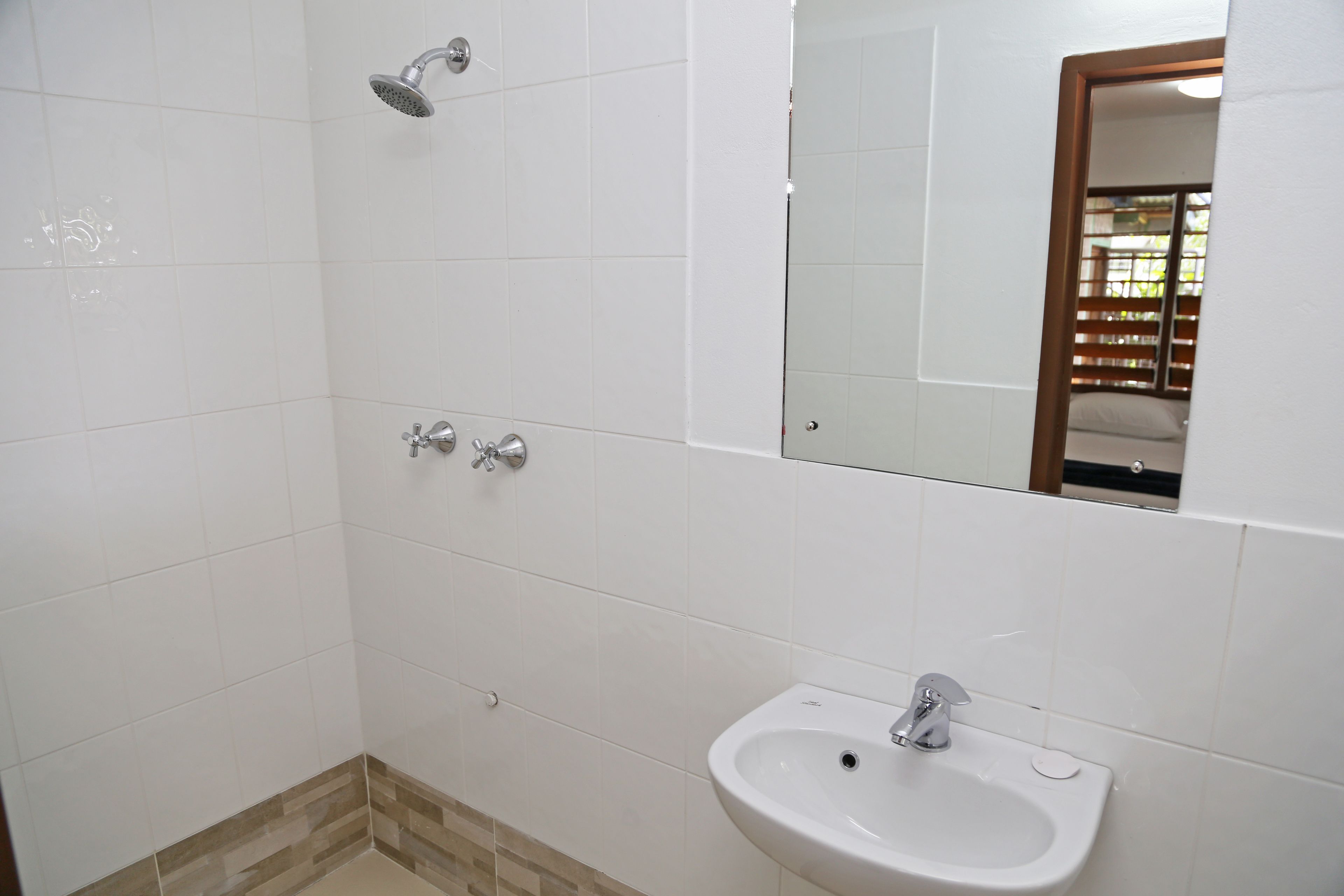 Casa de banho com azulejos brancos, uma pia e um chuveiro.