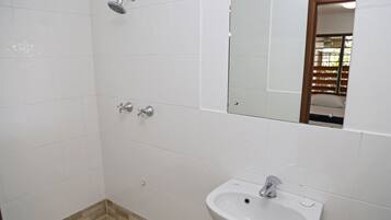 Casa de banho com azulejos brancos, uma pia e um chuveiro.
