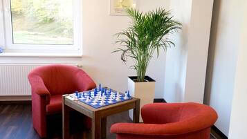 Quarto com duas poltronas vermelhas, uma mesa de madeira com um tabuleiro de xadrez e um vaso de planta.