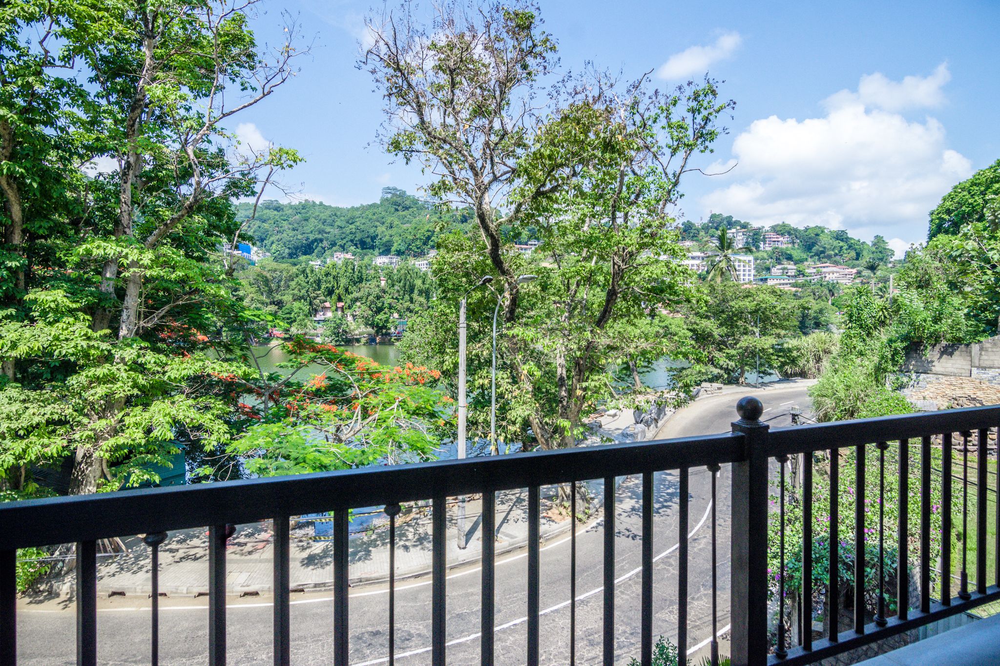 Vista de uma varanda com guarda-corpo, com vista para uma estrada, árvores e uma cidade ao longe.