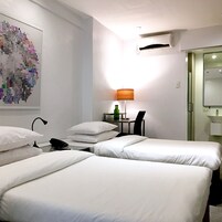 Quarto de hotel com duas camas, uma escrivaninha com luminária, um espelho e um aparelho de ar condicionado.