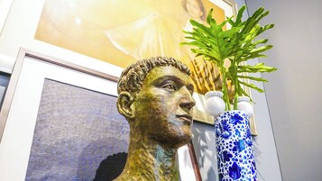 Uma estátua com superfície texturizada, uma obra de arte emoldurada e um vaso decorativo com uma planta.
