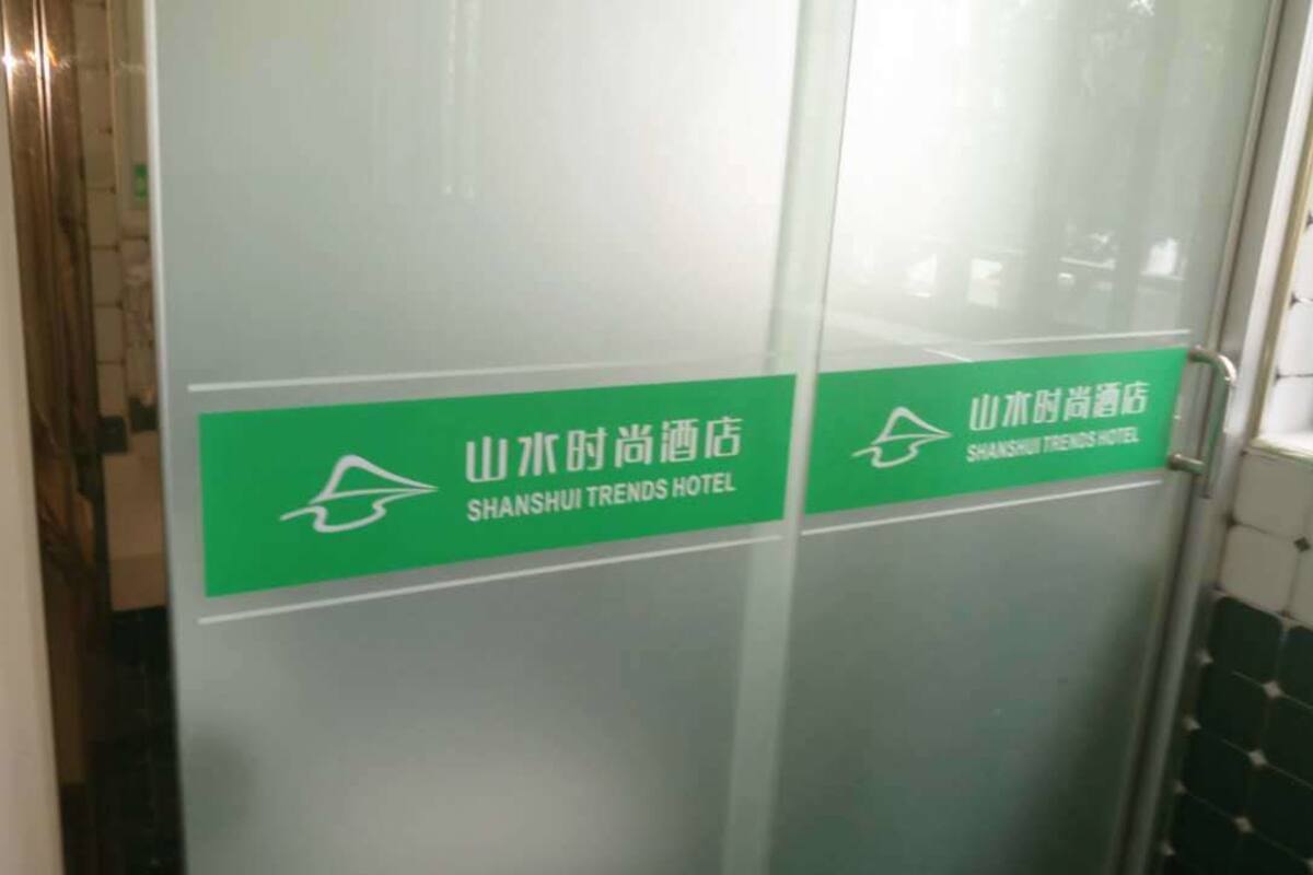 Entrada de hotel com uma placa verde indicando o nome 'Shenzhen Trends Hotel'.