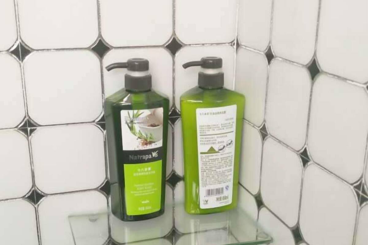 Casa de banho com paredes em azulejos brancos e pretos, uma prateleira de vidro com duas garrafas verdes e chão preto.