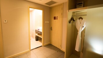 Quarto de hotel com guarda-roupa de madeira, banheiro com pia e espelho, e roupão pendurado em um suporte.