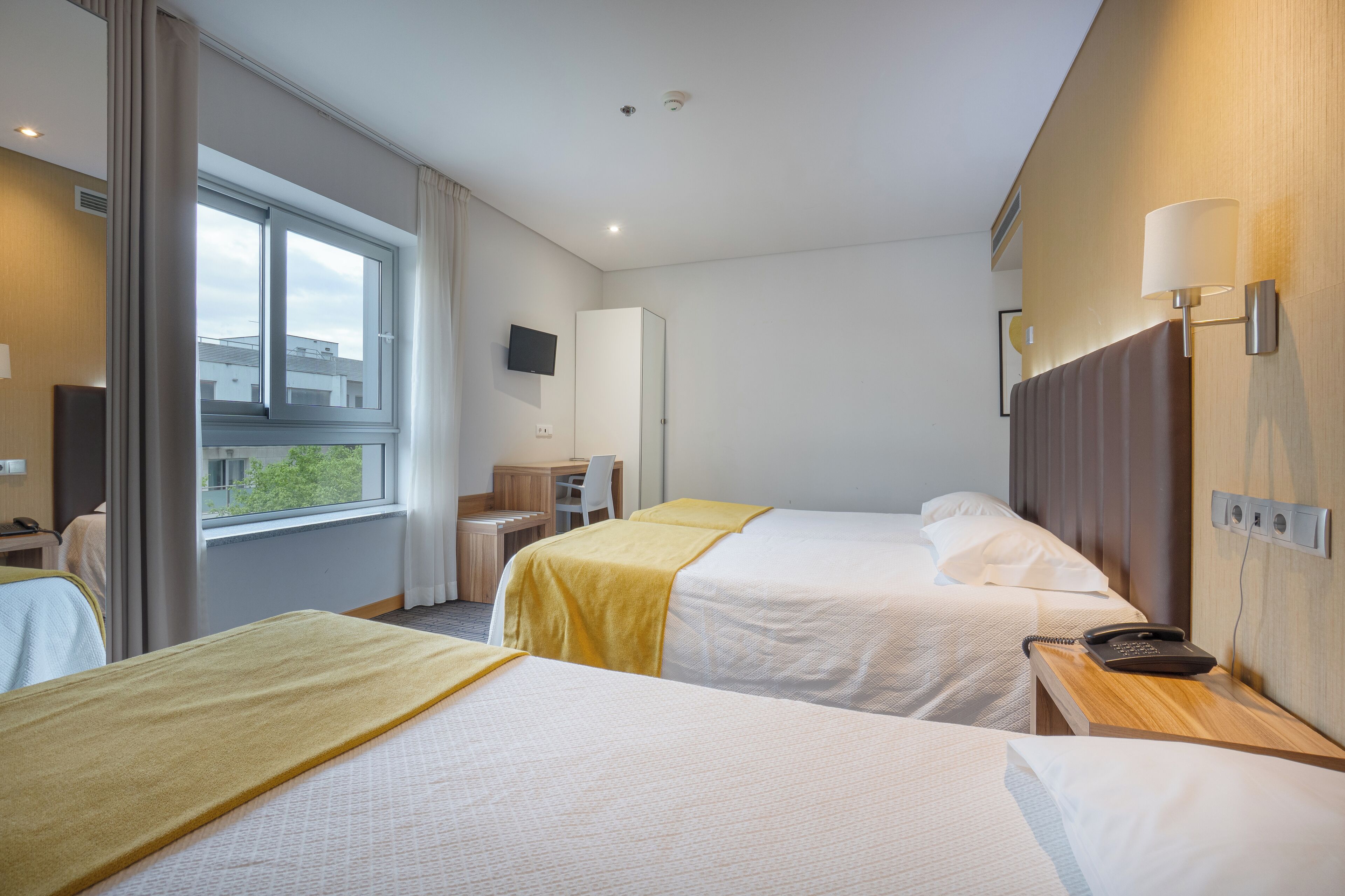 Quarto de hotel com duas camas, uma escrivaninha, uma cadeira, uma televisão e uma janela com cortinas.