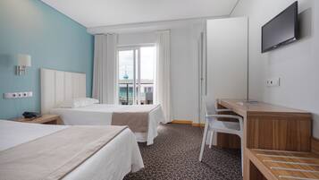 Quarto de hotel com duas camas, uma mesa, uma cadeira, uma televisão e uma janela com cortinas.