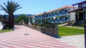 Um hotel com um caminho de azulejos que leva a um portão, rodeado por vegetação e palmeiras.