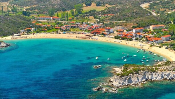 Vista aérea de uma cidade costeira com uma praia arenosa curvada, águas turquesa cristalinas e vários barcos.