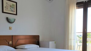 Quarto de hotel com duas camas, um ar condicionado pequeno, luminária fixada na parede e janela com cortinas.
