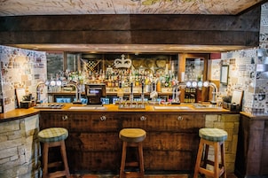 Um bar com balcão de madeira, banquetas e uma variedade de garrafas e copos.