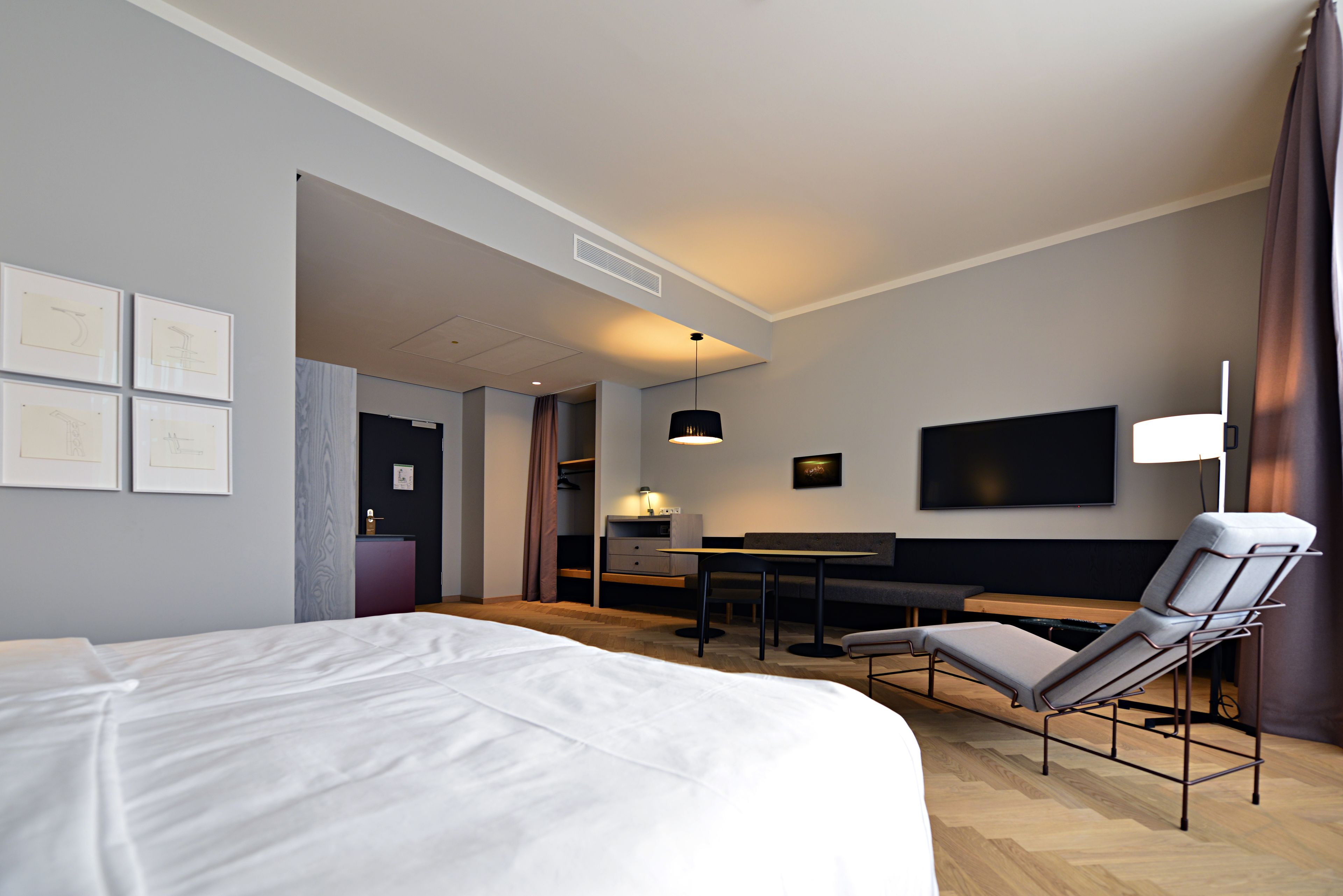 Quarto de hotel com cama, escrivaninha, cadeira, televisão e luminária.