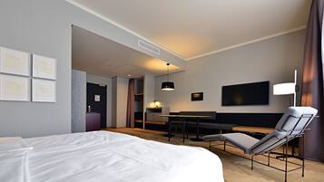 Quarto de hotel com cama, escrivaninha, cadeira, televisão e luminária.