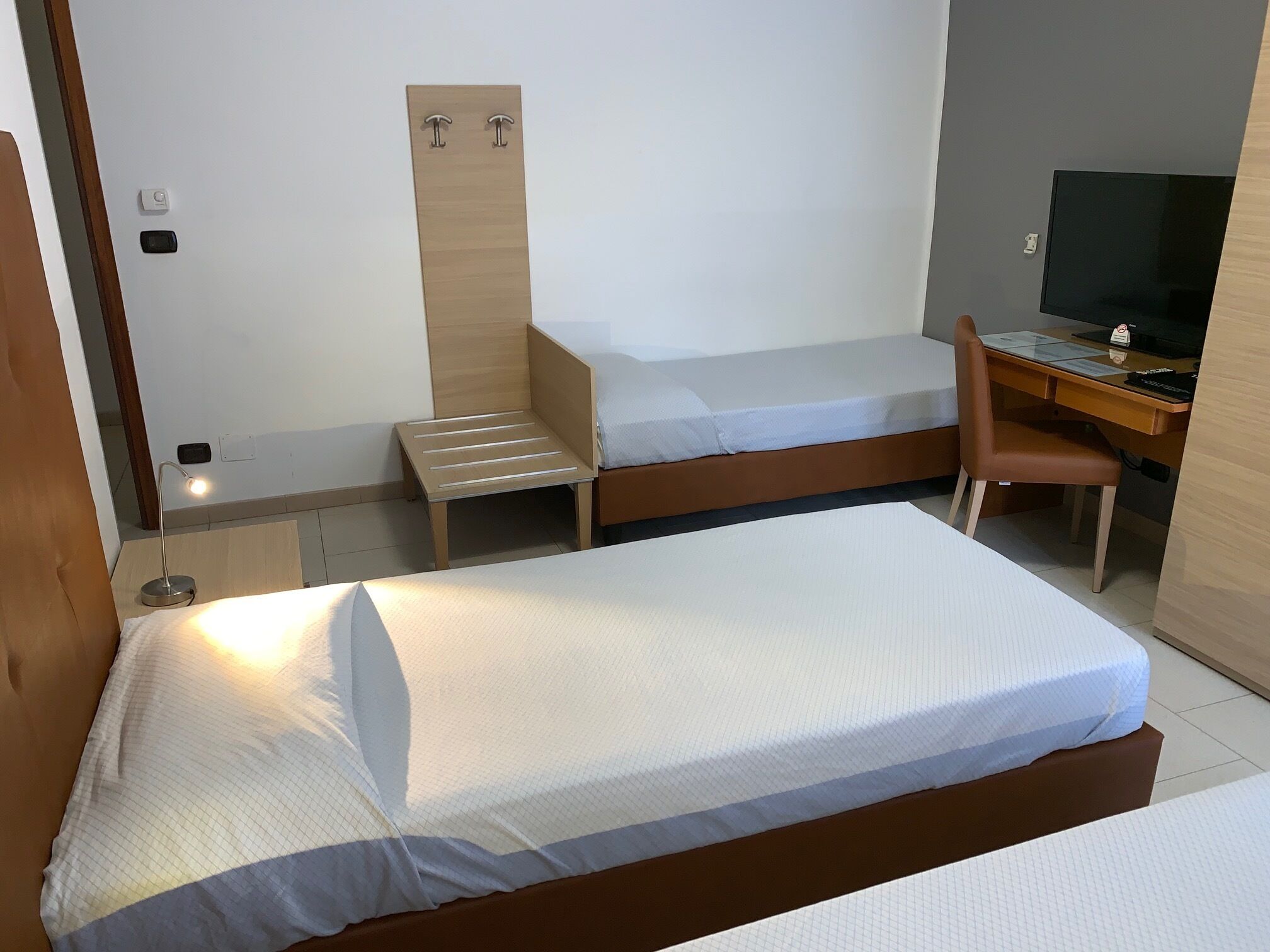 Quarto de hotel com duas camas de solteiro, uma escrivaninha com cadeira, televisão e guarda-roupa de madeira.