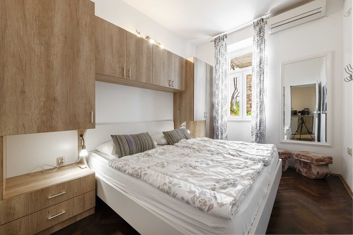 Um quarto com uma cama, armários de madeira, uma mesa de cabeceira e uma janela com cortinas.