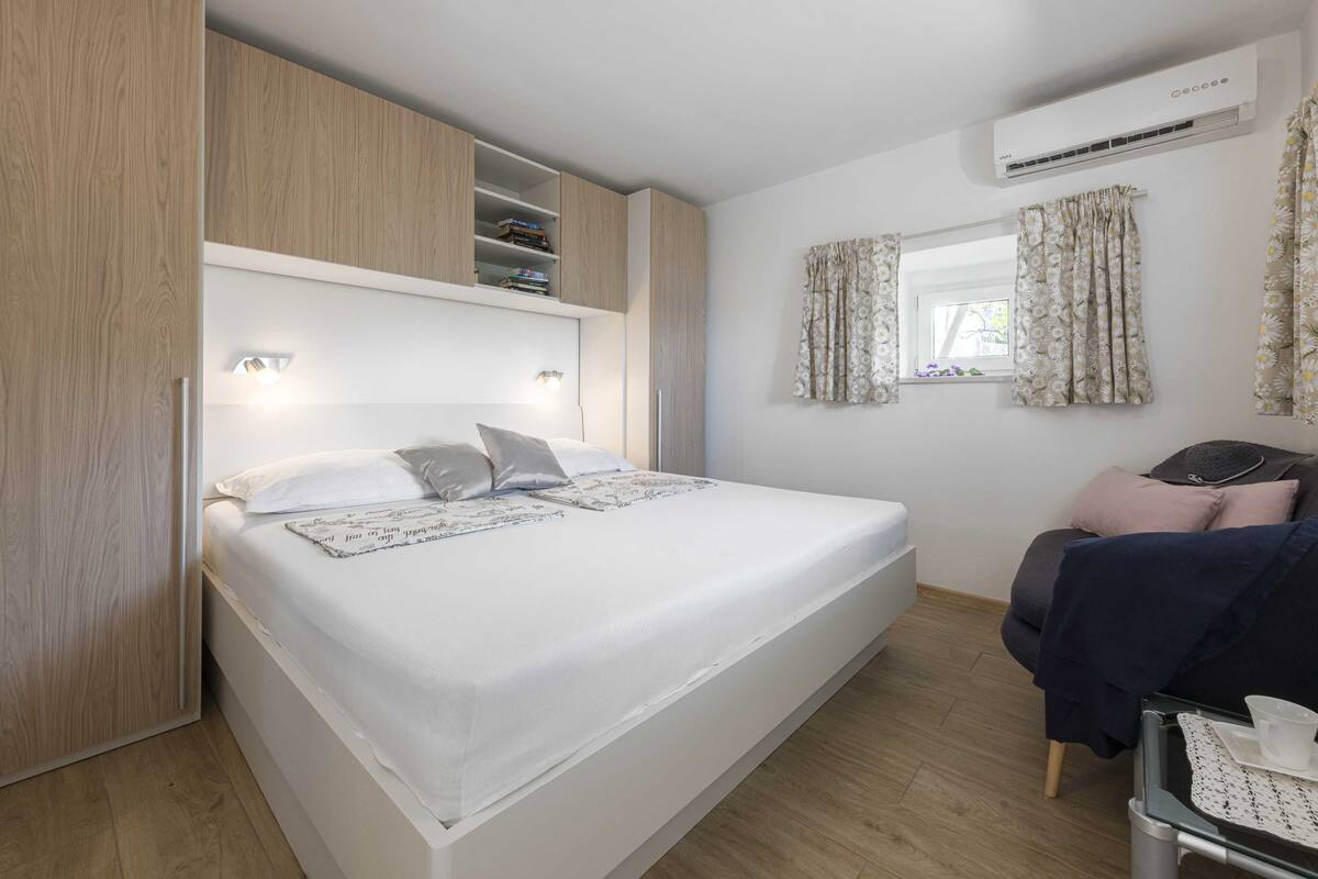 Quarto moderno com cama grande, roupeiro embutido e um pequeno espaço para sentar.