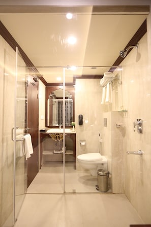 Uma casa de banho moderna com chuveiro em cabine de vidro, toucador com espelho, sanita e um contentor de lixo.