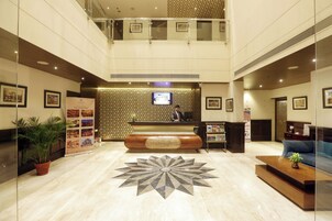 Um saguão de hotel com balcão de recepção, um amplo padrão decorativo no chão, área de estar e quadros nas paredes.