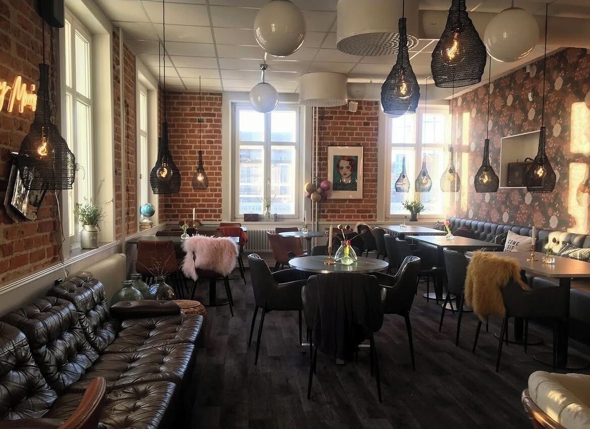 Um restaurante acolhedor com paredes de tijolo, assentos de couro, luminárias pendentes e uma janela grande.
