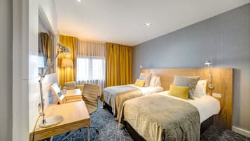 Quarto de hotel com duas camas, uma escrivaninha, uma cadeira e um abajur.