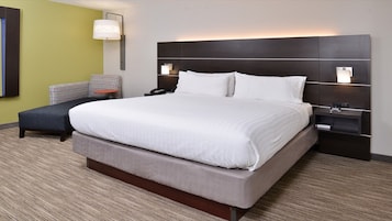 Quarto de hotel com uma cama grande, mesa de cabeceira, uma cadeira e uma luminária.