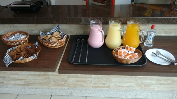 Um buffet de café da manhã com diversas bebidas, doces e acompanhamentos em uma bandeja.